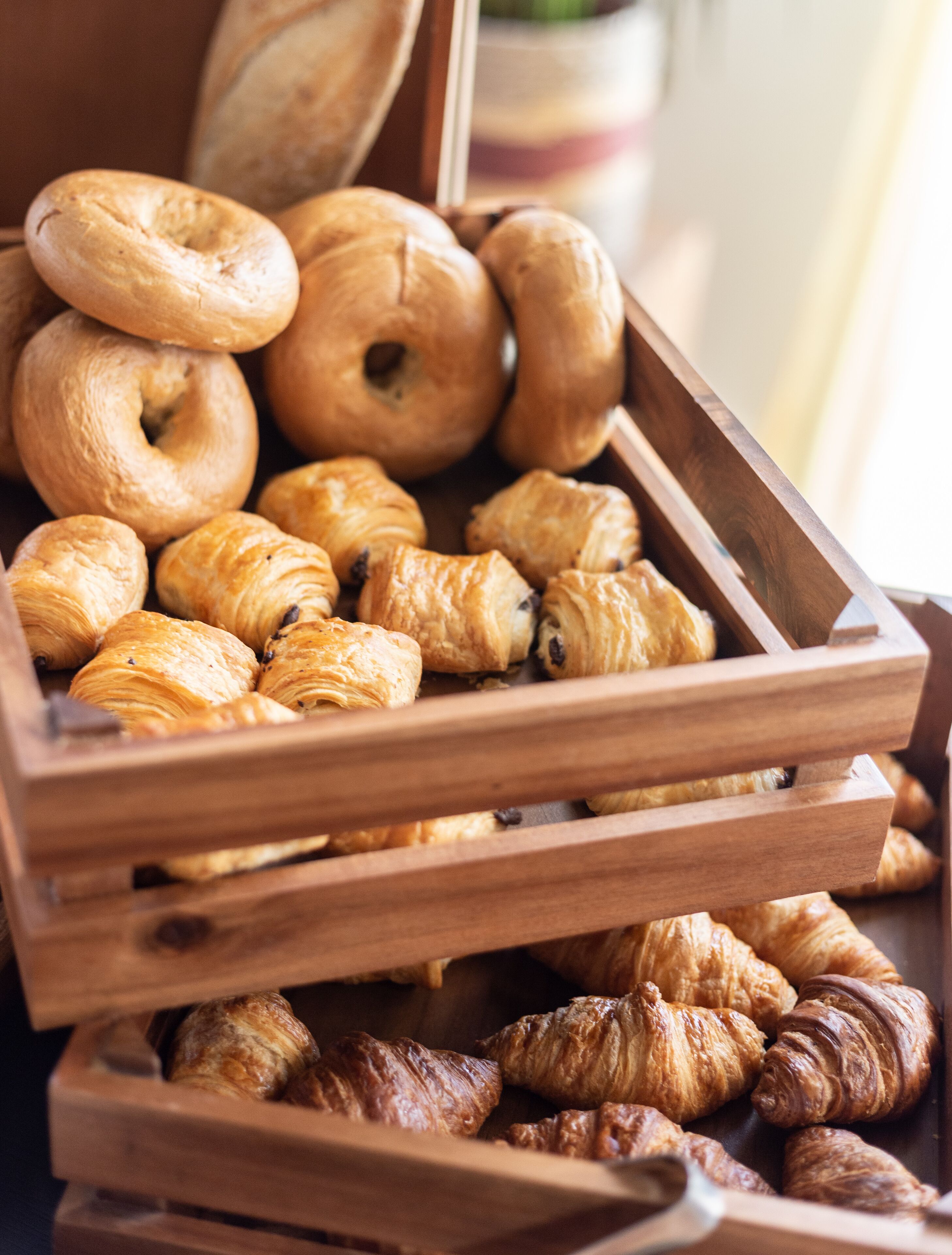 Uma caixa de madeira cheia de diferentes tipos de pastelaria, incluindo bagels e croissants.