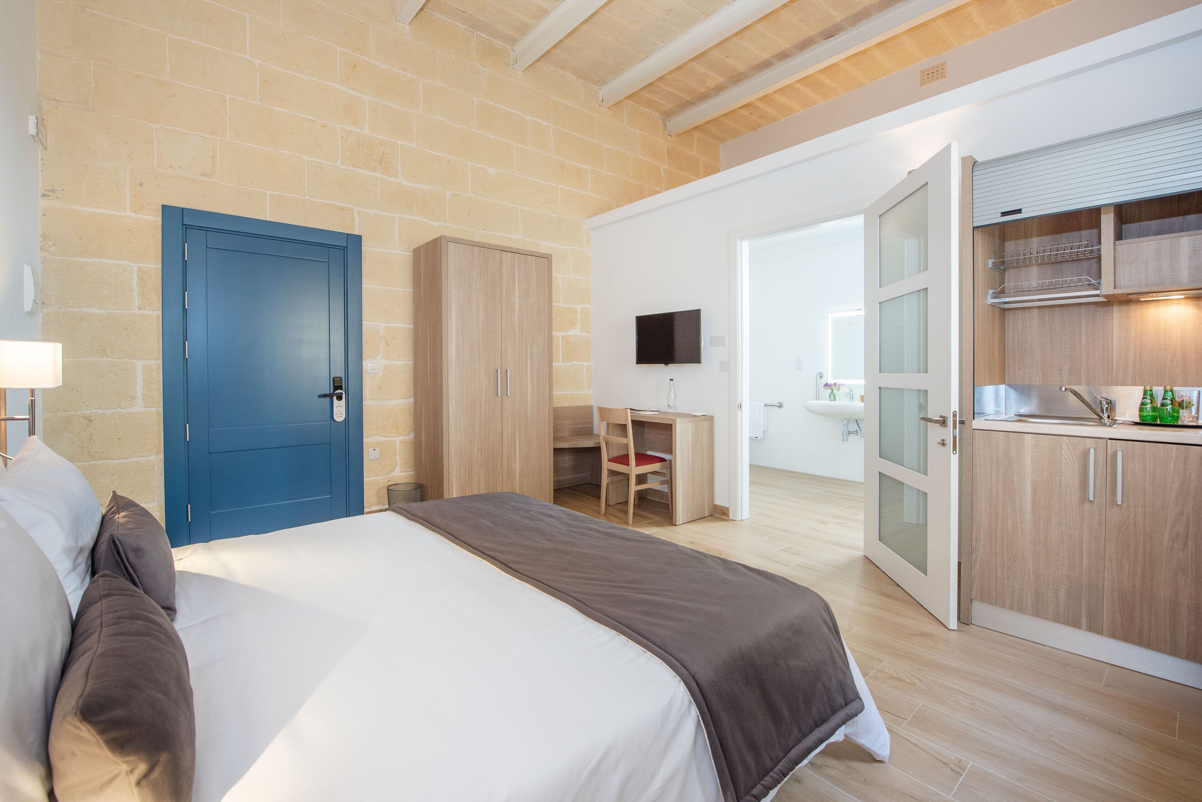 Quarto com cama, escrivaninha e cozinha compacta.