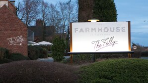 Placa de 'The Folly Farmhouse' em Mackworth, com um edifício de tijolos e uma sebe bem cuidada em primeiro plano.