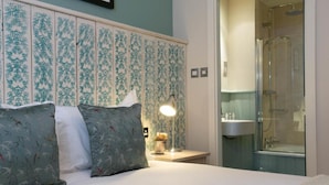 Quarto de hotel com uma cama, uma mesa de cabeceira com abajur e área de chuveiro.