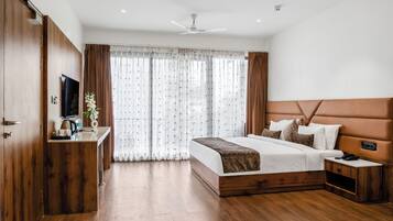Um quarto moderno com piso de madeira, uma cama com cabeceira, mesa de cabeceira, luminária de apoio e uma janela com cortinas.