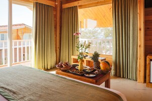 Quarto de cabana de madeira com cama, uma mesa de jantar com itens de café da manhã e vista para um deck de madeira lá fora.