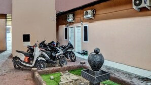 Pátio com várias scooters estacionadas, um vaso de pedra decorativo e aparelhos de ar condicionado na parede.