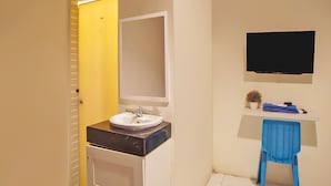 Casa de banho com lavatório branco, espelho, bancada preta, cadeira azul e um armário com produtos de higiene pessoal.