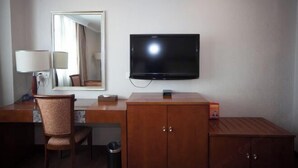 Quarto de hotel com uma mesa de madeira, uma cadeira, televisão fixada na parede e espelho sobre a mesa.