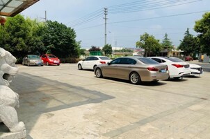 Um estacionamento com vários carros, uma est átua e árvores ao fundo.