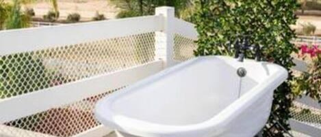 Uma banheira branca sobre um piso de concreto com um tapete de boas-vindas à frente.