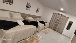 Quarto de hotel moderno com duas camas, televisão de tela plana e uma janela grande com cortinas.