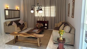 Uma sala de estar com dois sofás, uma mesa de centro, uma mesa lateral, um candelabro e um espelho grande.