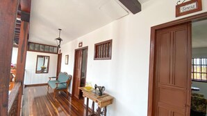 Um corredor com piso de madeira, uma cadeira, uma máquina de costura sobre uma mesa e uma porta com a placa 'Teresa'.