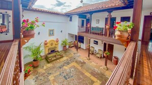 Um pátio com piso de azulejos, plantas em vasos e uma varanda de madeira.
