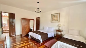 Quarto de hotel com duas camas, piso de madeira, um candelabro, um quadro na parede e uma pequena mesa com abajur.