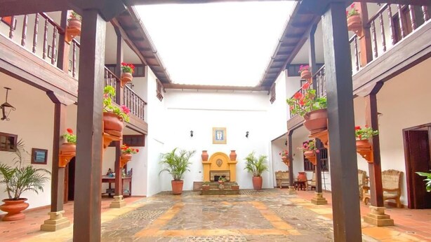 Pátio com uma fonte central, rodeado por vasos de plantas e chão de pedra.