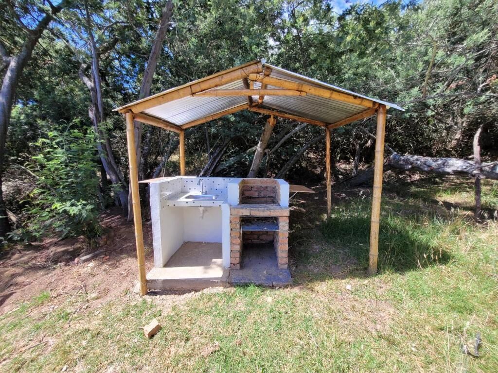 Uma estrutura de madeira com telhado de metal, possivelmente um gazebo ou abrigo, em uma área arborizada.