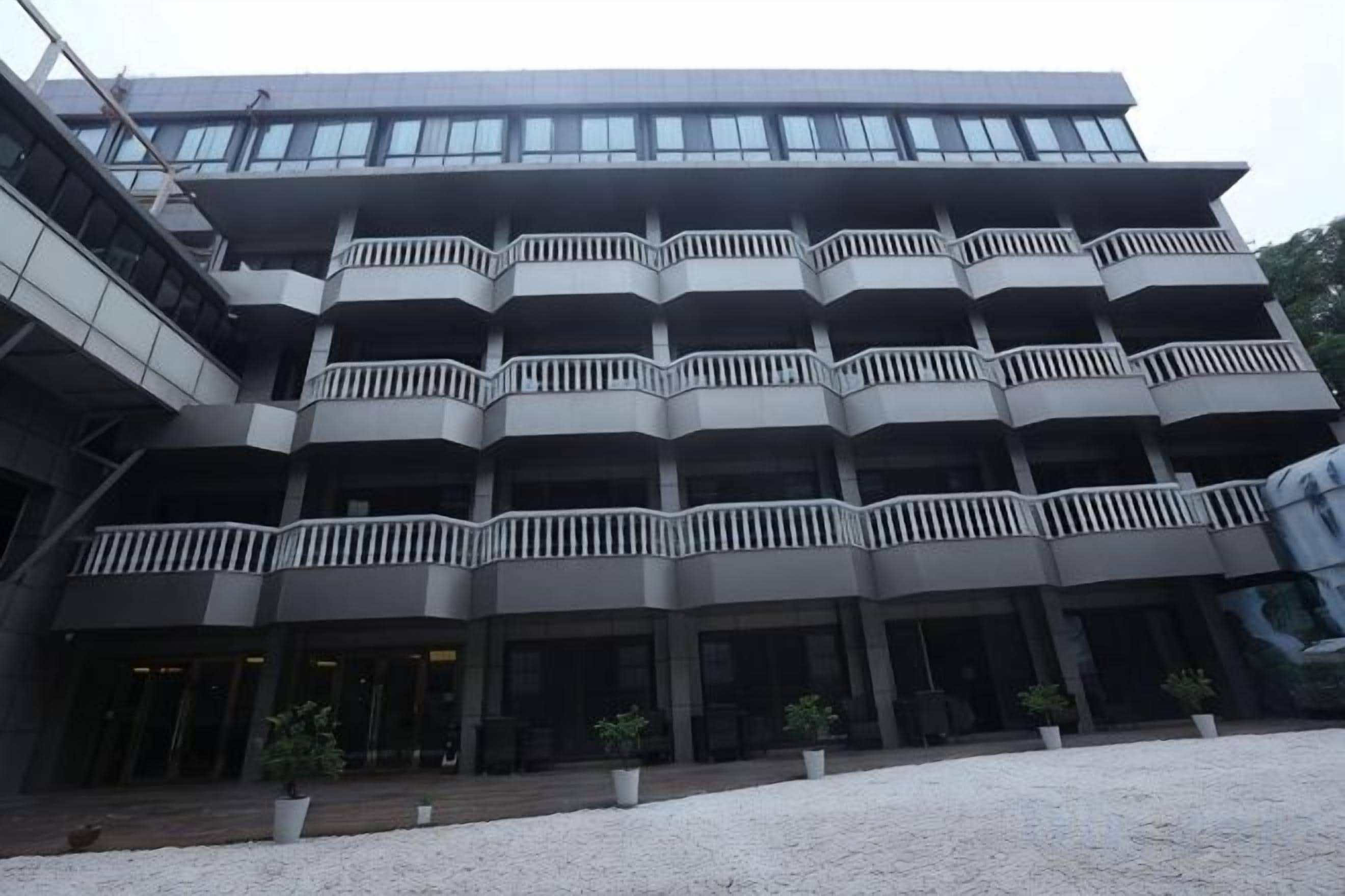 Um edifício com várias andares, sacadas, entrada coberta e plantas em vasos.