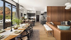 Cozinha moderna com armários escuros, uma ilha central e uma área de jantar com uma mesa comprida e cadeiras.