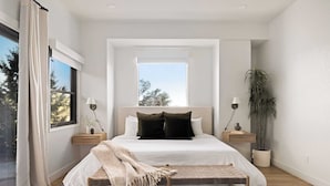 Quarto moderno com uma cama grande, mesas de cabeceira, um banco e uma janela.