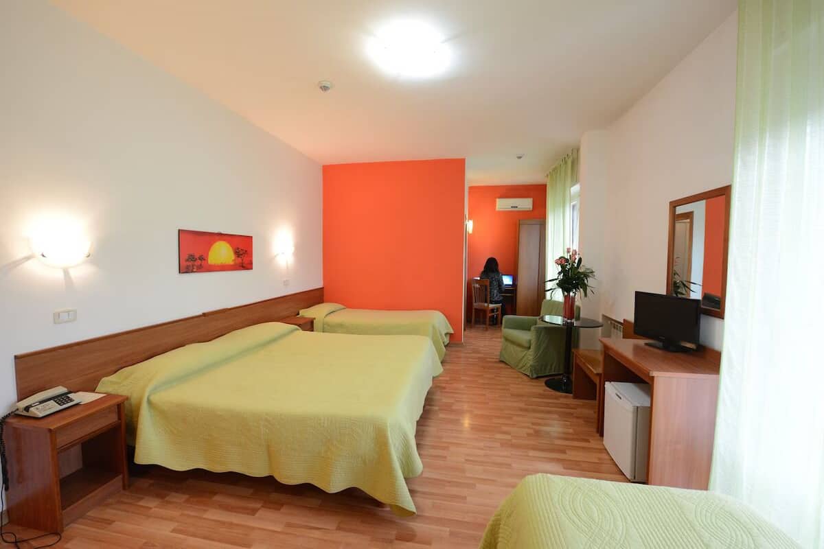 Quarto de hotel com duas camas, uma escrivaninha com computador, uma cadeira, um pequeno frigorífico e um telefone na mesa de cabeceira.