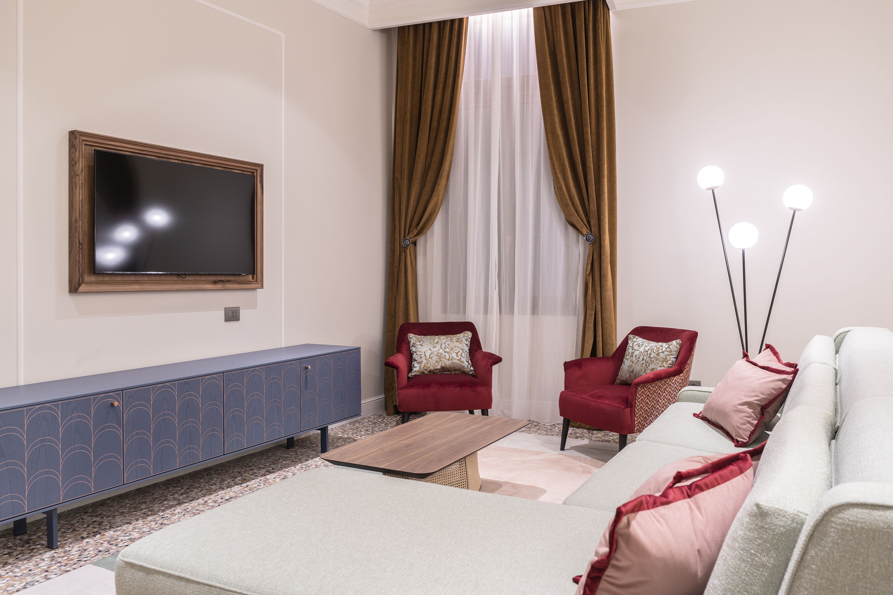Uma sala de estar moderna com uma televisão de tela plana, um sofá, duas poltronas, uma mesa de centro e um console azul.