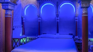 Quarto com uma cama grande, arcos elaborados e detalhes intrincados nas paredes.