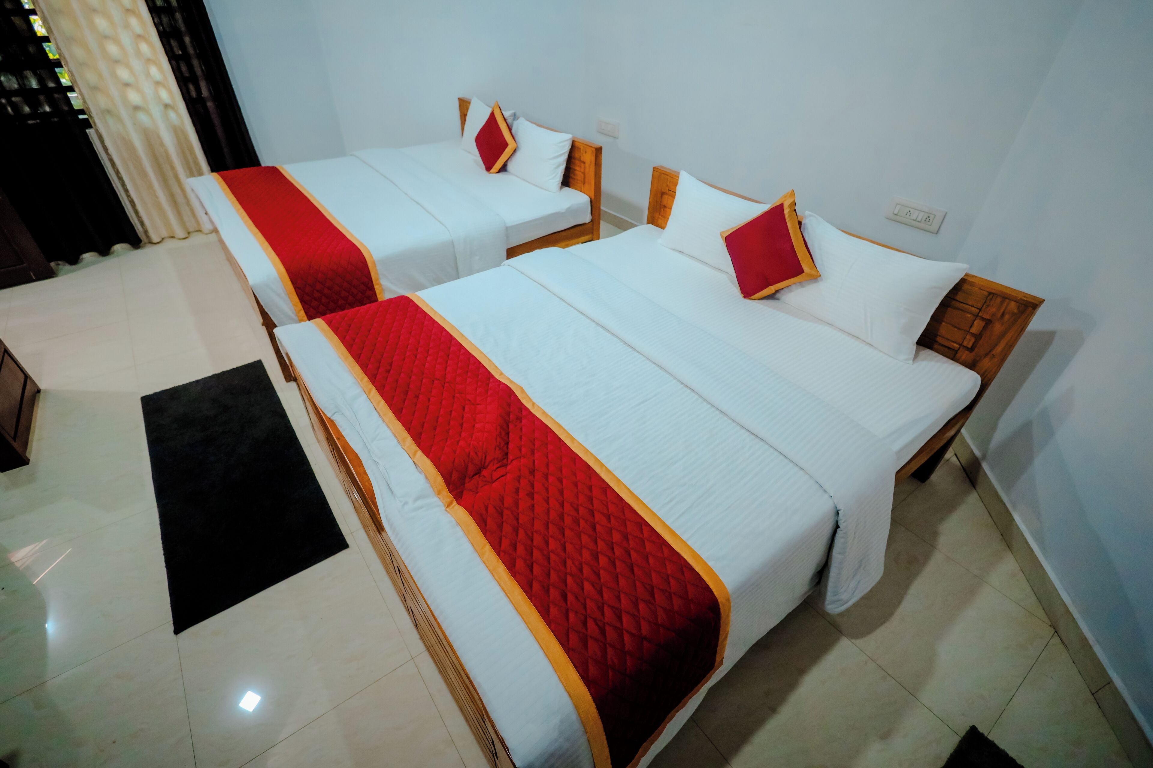 Quarto de hotel com duas camas, cada uma com colcha vermelha e branca, e um tapete preto no chão.