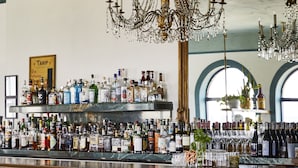 Uma área de bar com balcão de madeira, dois bancos, um candelabro e um espelho.