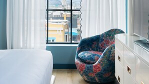 Quarto com cama, cadeira, televisão e janela com cortinas.