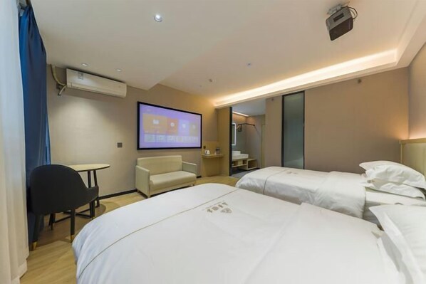 Quarto de hotel com duas camas, uma escrivaninha, uma cadeira, uma televisão e um espelho.