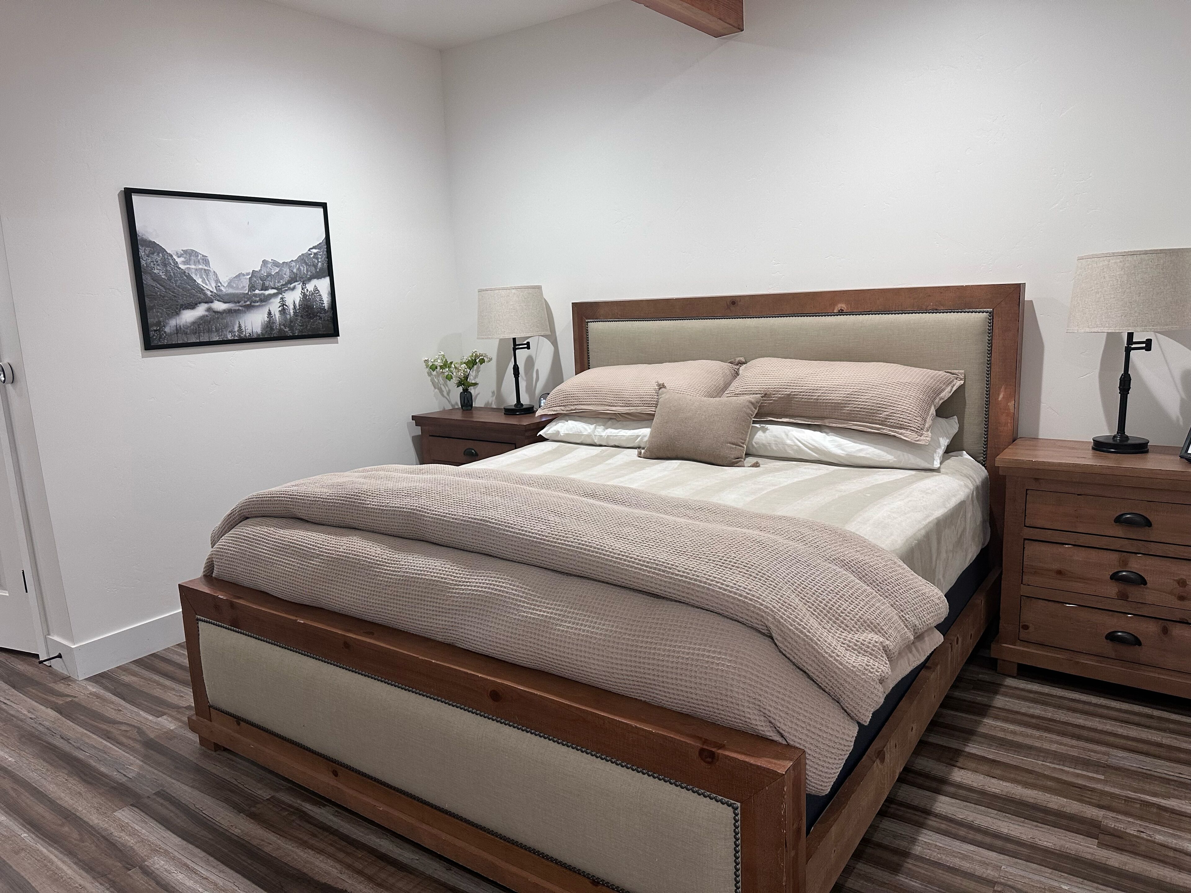 Uma cama bem arrumada com cabeceira de madeira, uma mesa de cabeceira com abajur e um quadro na parede.
