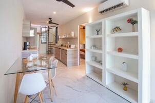Uma cozinha moderna com uma mesa de jantar de vidro, cadeiras brancas e uma estante branca com objetos decorativos.