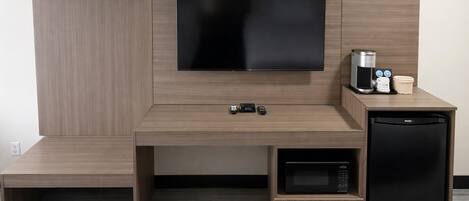 Uma cozinha compacta moderna com televisão integrada, cafeteira, micro-ondas e frigorífico.