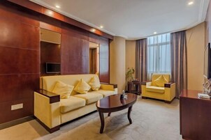 Uma sala de estar moderna com sofá, poltrona e mesa de centro, uma televisão de tela plana e uma grande janela com cortinas.