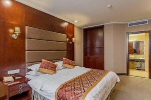 Quarto de hotel com uma cama grande, cabeceira de madeira, mesa de cabeceira com abajur e guarda-roupa.