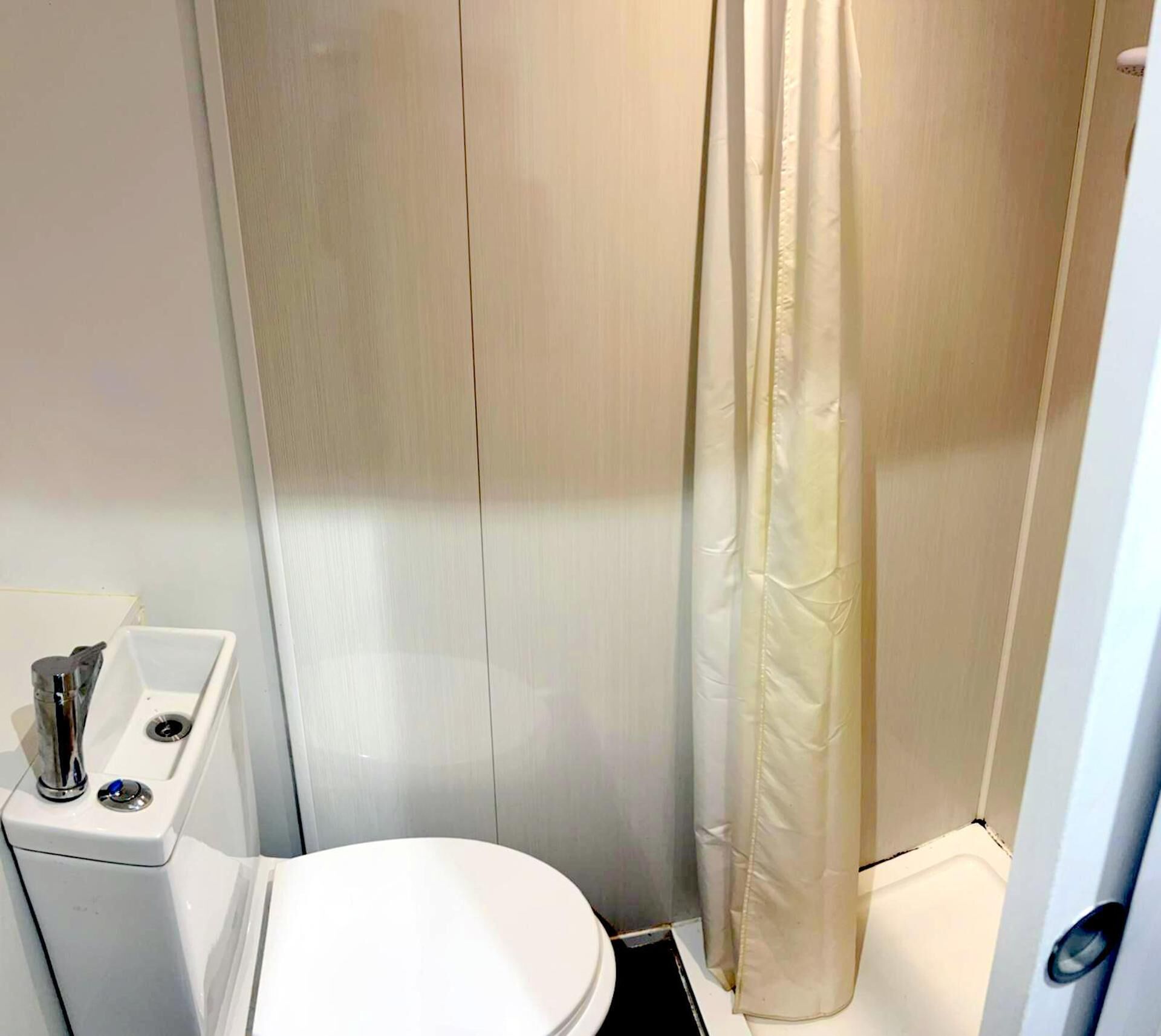 Um banheiro pequeno e compacto, com vaso sanitário branco, pia com torneira cromada e cortina de chuveiro.