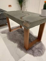 Uma mesa de concreto com pernas de madeira e um tapete felpudo por baixo.