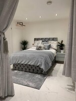 Quarto com cabeceira estofada, colcha e tapete cinzas.