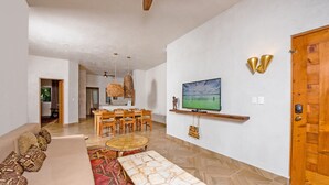 Ampla sala de estar com sofá, mesa de jantar e TV fixada na parede.