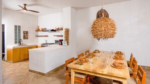 Cozinha moderna com ilha central, mesa de jantar de madeira posta com pratos e copos, e luminária pendente.
