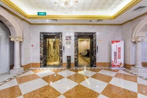 Um saguão de hotel com piso xadrez, paredes de mármore e dois elevadores.
