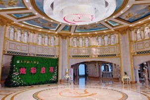 Um amplo saguão de hotel com piso de mármore circular, um lustre imponente e um painel floral verde com caracteres chineses.