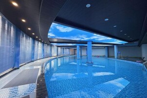 Piscina interna com design curvo, teto com padrão que imita o céu e piso revestido de azulejos.