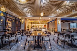 Ampla sala de jantar com uma mesa comprida e várias cadeiras, área de bar com banquetas e design moderno no teto.