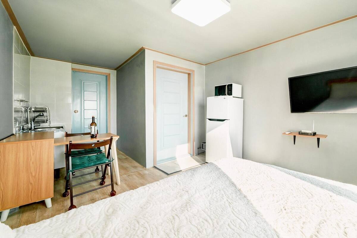 Quarto de hotel com cama, escrivaninha, cadeira, micro-ondas, televisão e prateleira pequena.