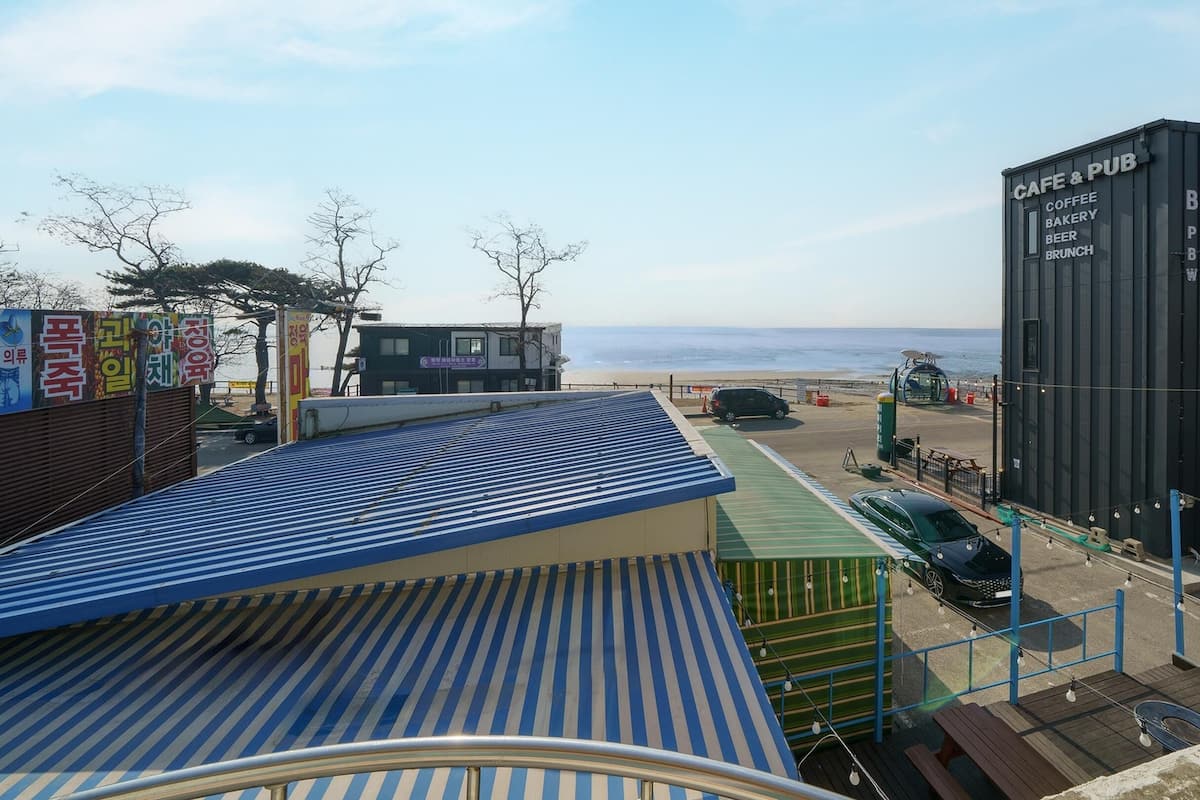 Vista costeira com um café e uma padaria, área de estacionamento e uma praia ao fundo.