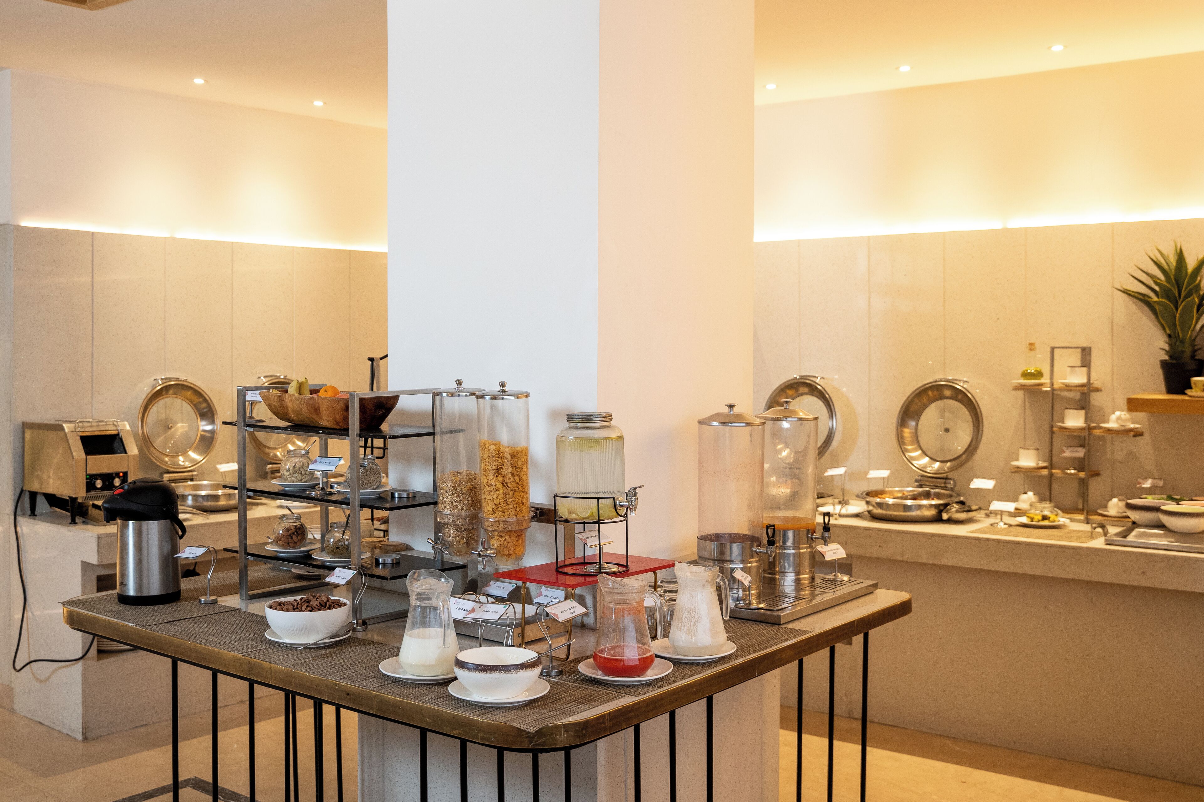 Disposição de buffet com diversos alimentos e bebidas, incluindo tigelas, jarras e uma máquina de café.