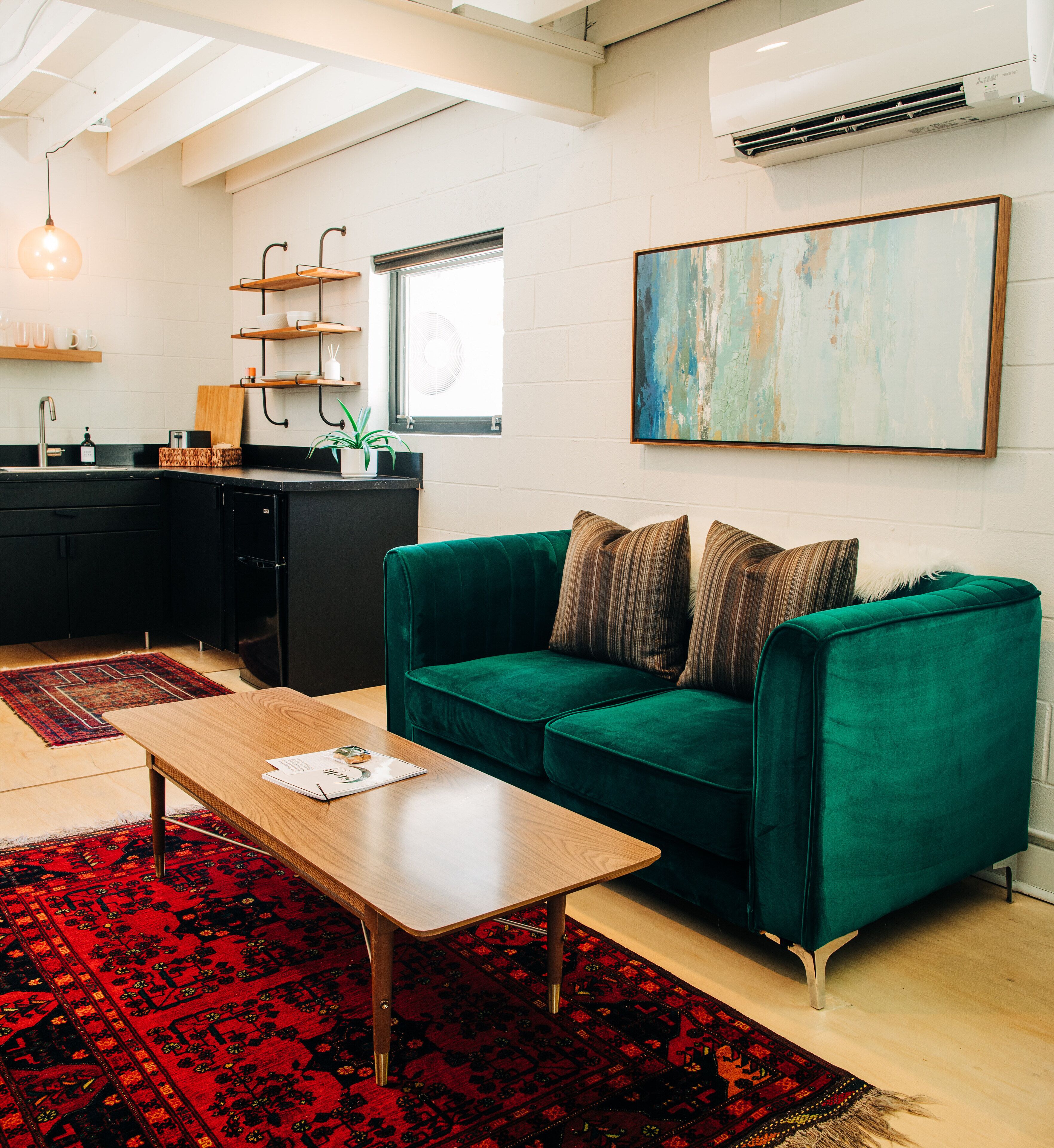 Uma sala de estar moderna com um sofá verde, mesa de centro de madeira e um tapete vermelho estampado.