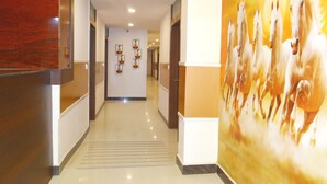 Corredor de hotel com piso lustroso, uma escultura na parede e um grande mural de cavalos.