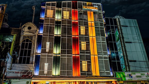 Um hotel bem iluminado com uma placa de destaque com o nome "ALHAMBRA" e uma entrada visível com toldo verde.