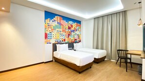 Quarto de hotel moderno com duas camas, uma escrivaninha e um mural colorido com vista para a cidade.