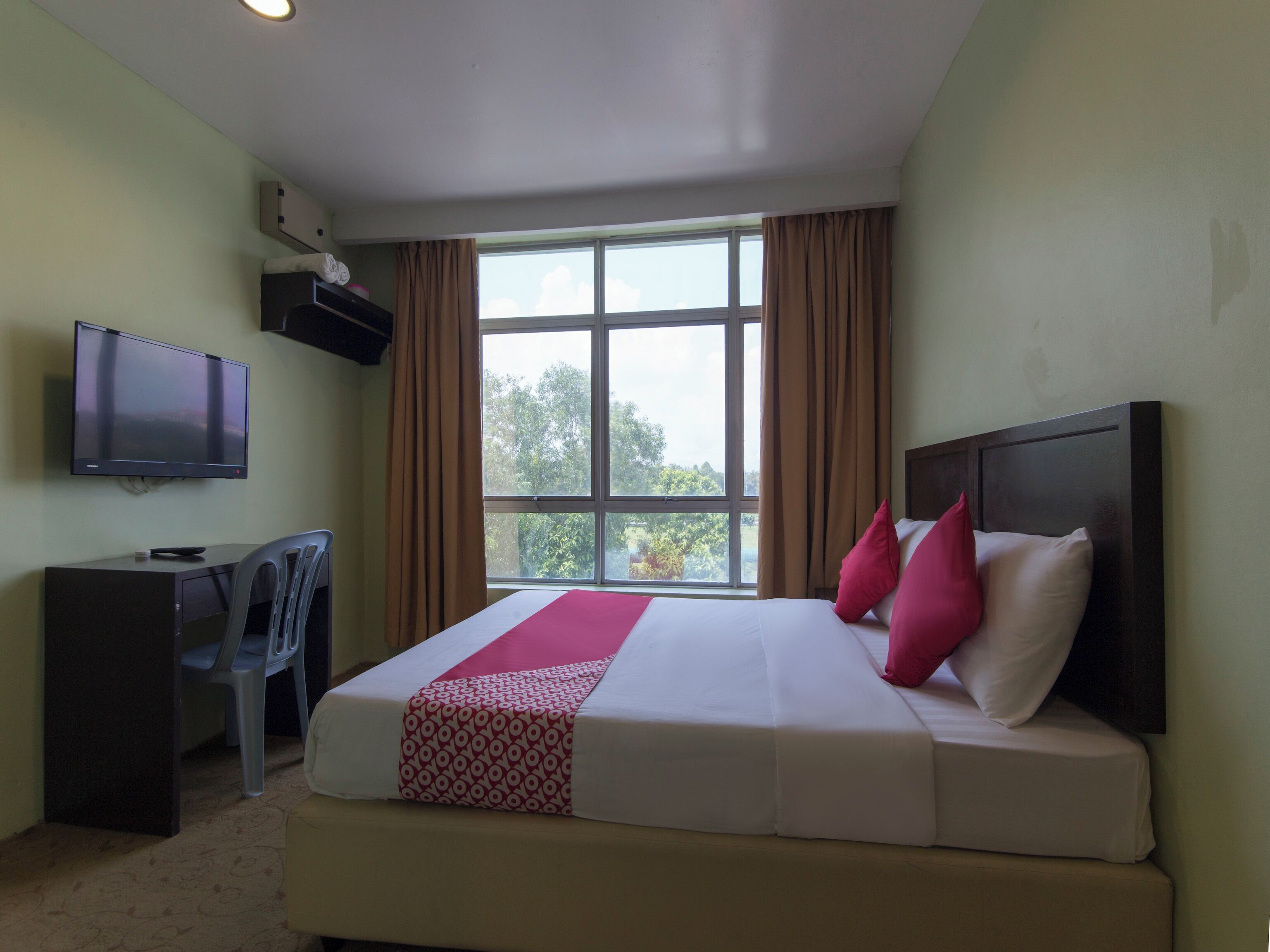 Quarto de hotel com cama, escrivaninha, cadeira, televisão e janela com cortinas.